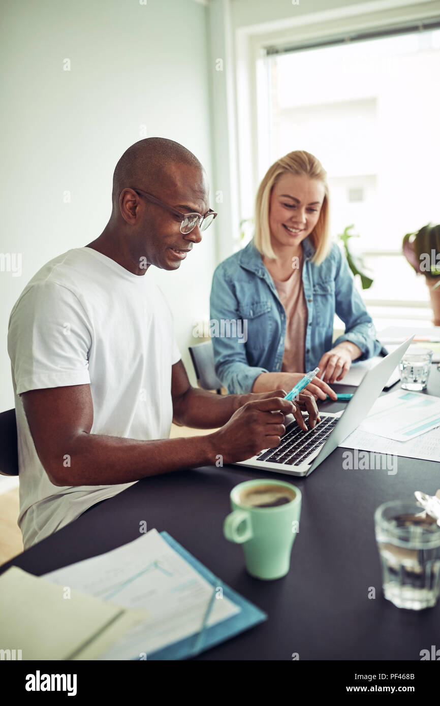 Two smiling diverse coworkers talking together over a laptop while ...