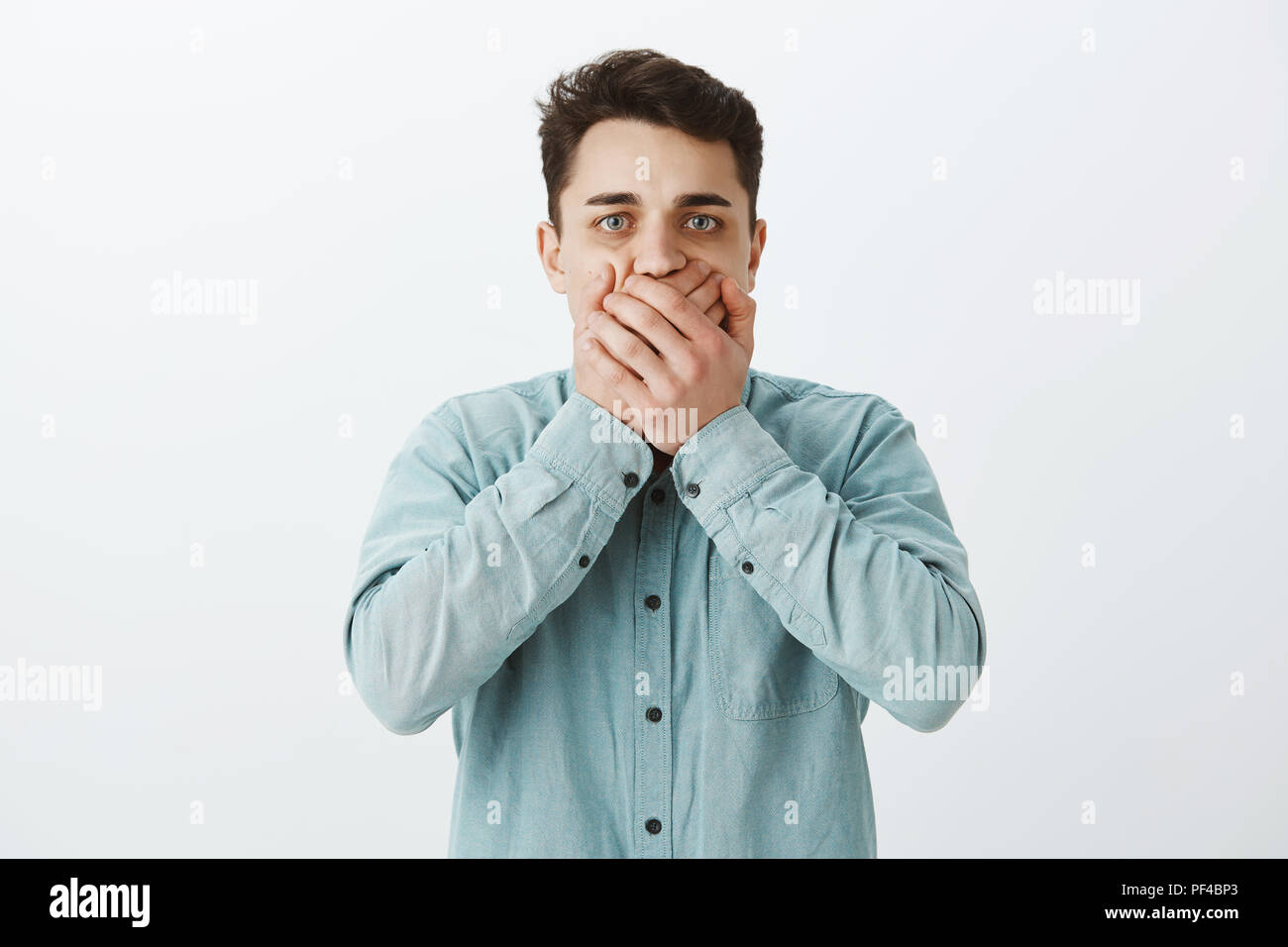 Studio shot of uncomfortable worried caucasian man in shirt, covering ...