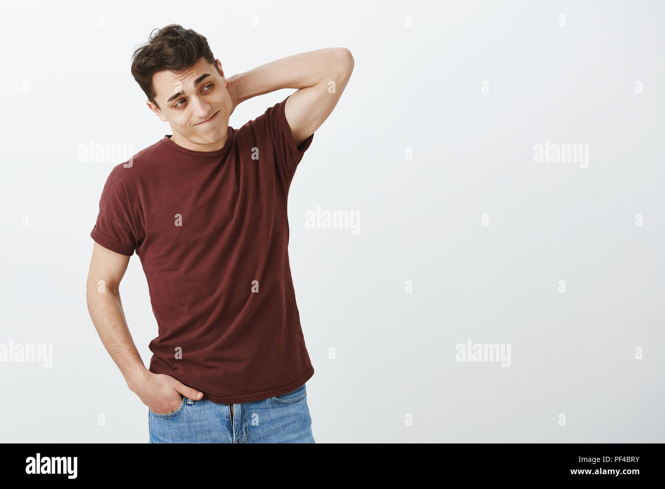 Studio shot of unsure doubtful handsome guy, touching back of head and ...