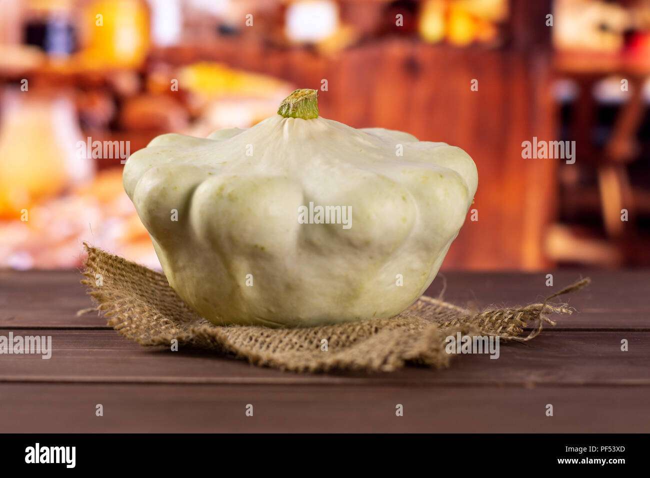 One whole summer white pattypan squash on linen cloth with rustic wood kitchen in background ...