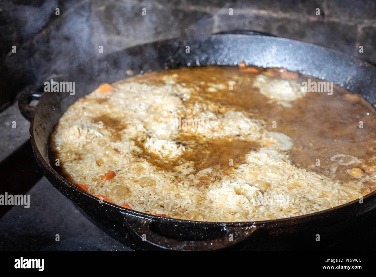 cooking Rice for pilaw or paella in iron cauldron over open fire. Smoke ...