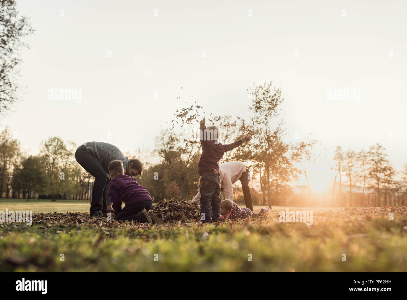 Retro image of family rejoicing in an autumn sunset throwing leaves in ...