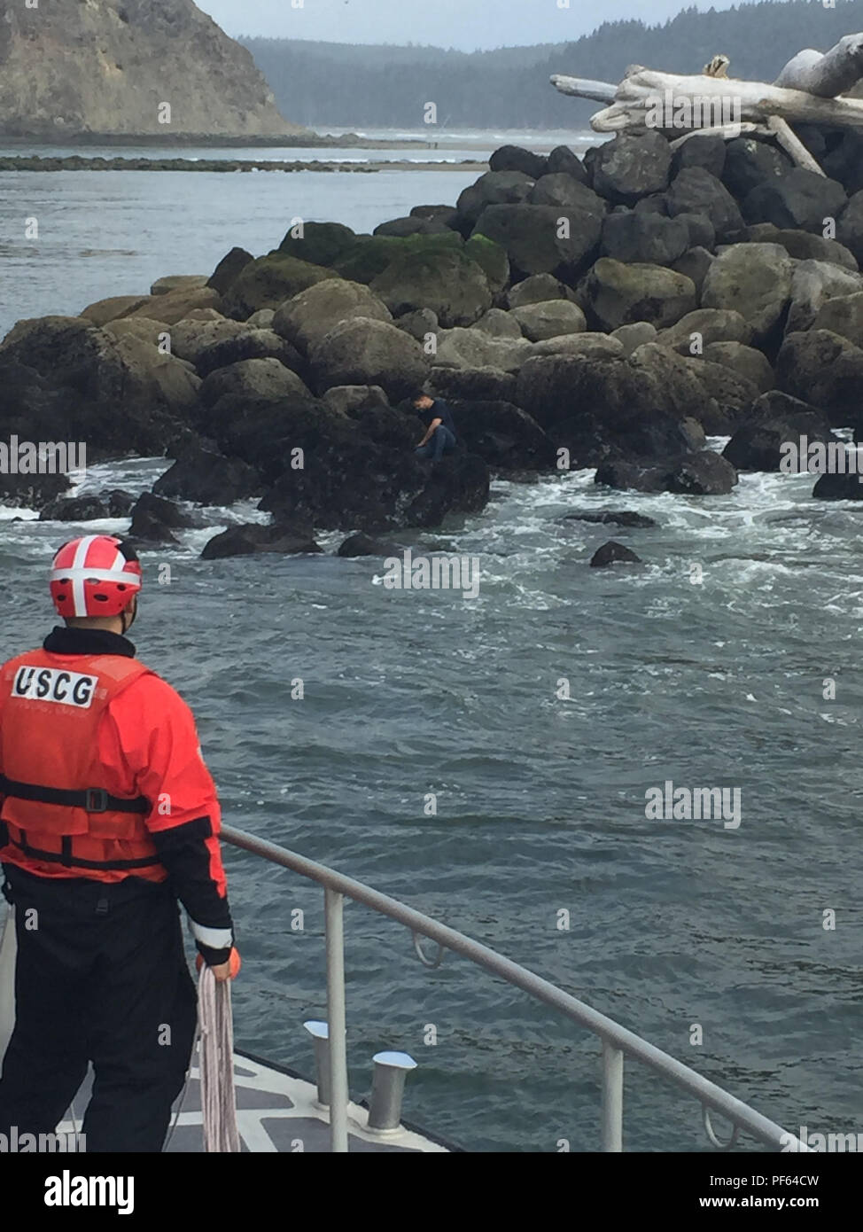 An injured swimmer sits on rocks as a Coast Guard boat crew aboard a 47 ...