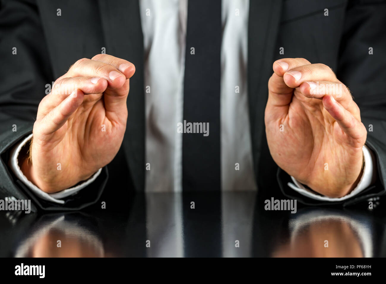 Businessman in a suit sitting at a desk making a protective gesture ...