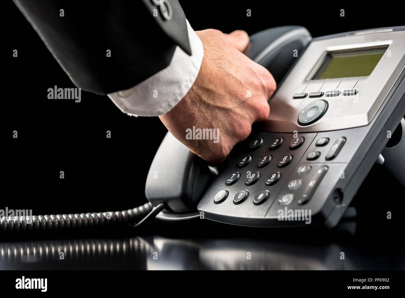 Businessman making a call on a landline telephone lifting the handset ...