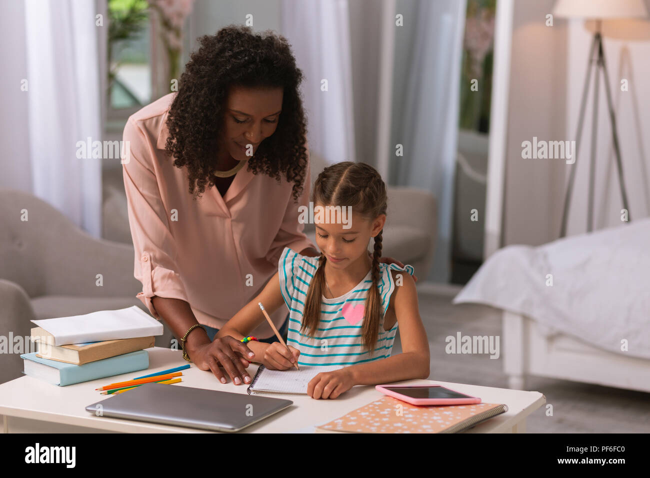 Positive smart little girl writing with mother Stock Photo - Alamy