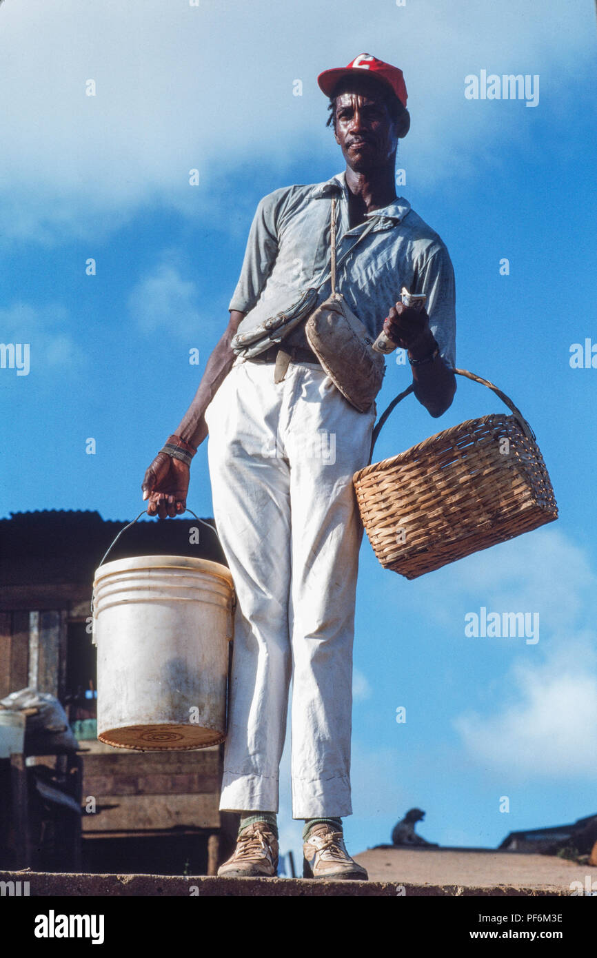 A man carrying containers, including a basket and a plastic bucket ...