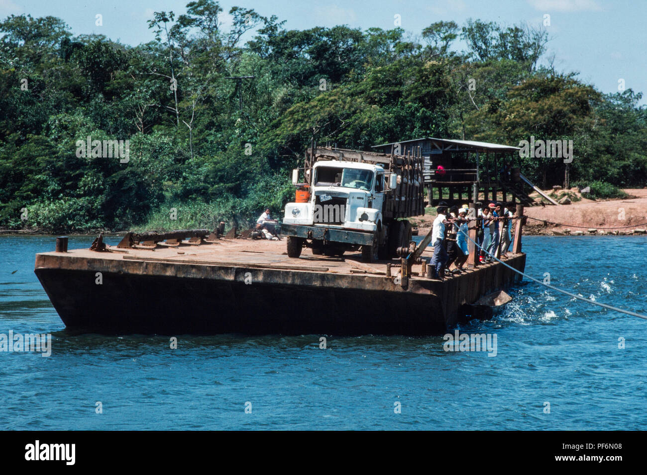 A truck aboard a river ferry crossing in a tropical forest region, with ...