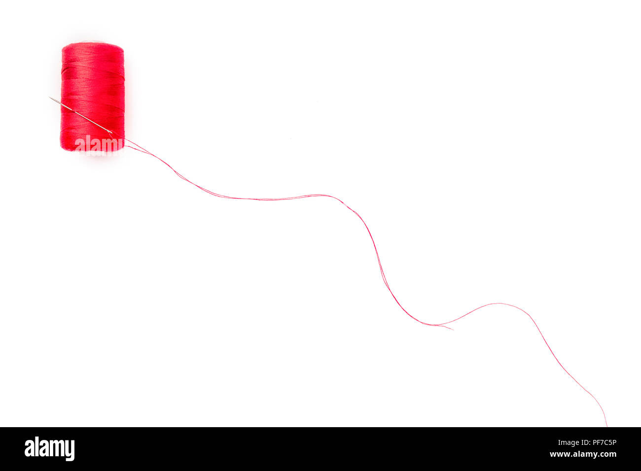 Overhead photo of a needle with a red thread and a spool on a white ...