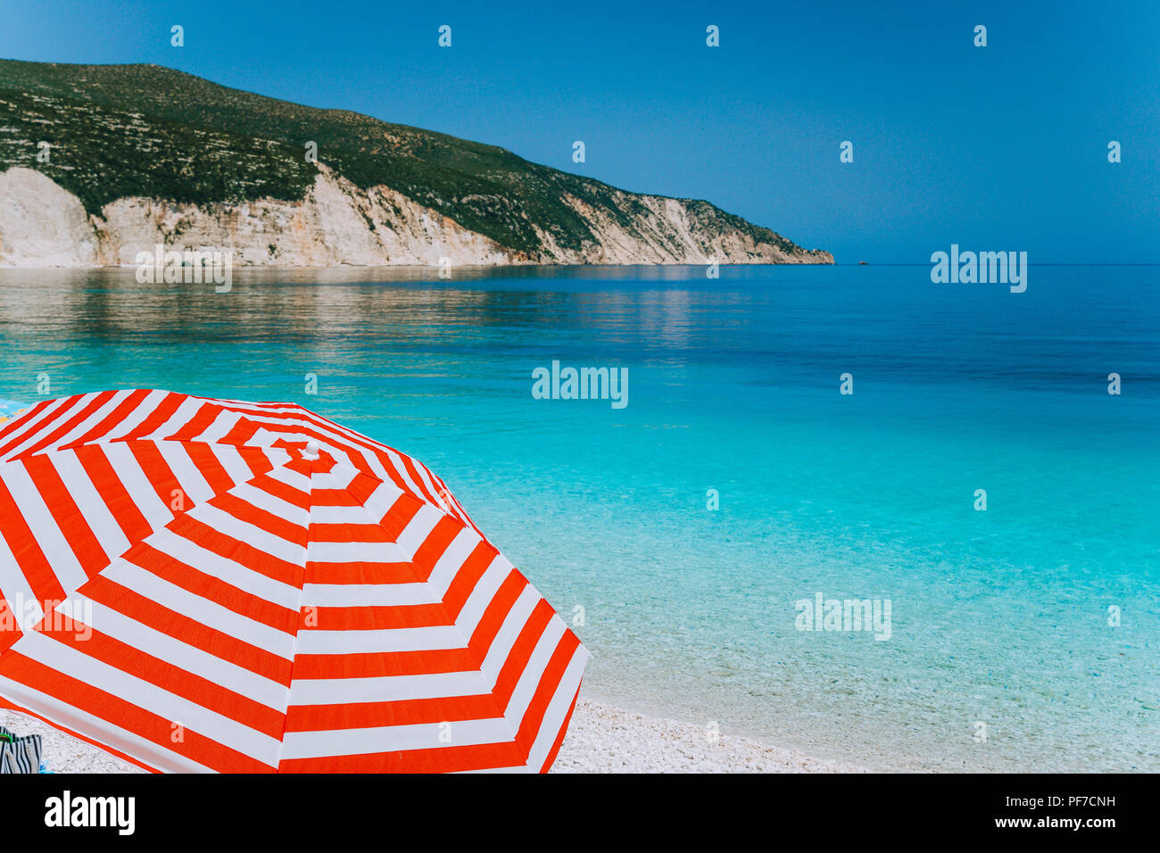 Bright red striped sun beach umbrella on beach against turquoise blue ...