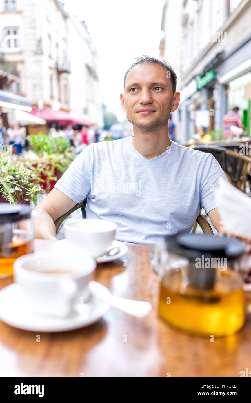 Young happy man sitting in European outdoor cafe restaurant looking ...