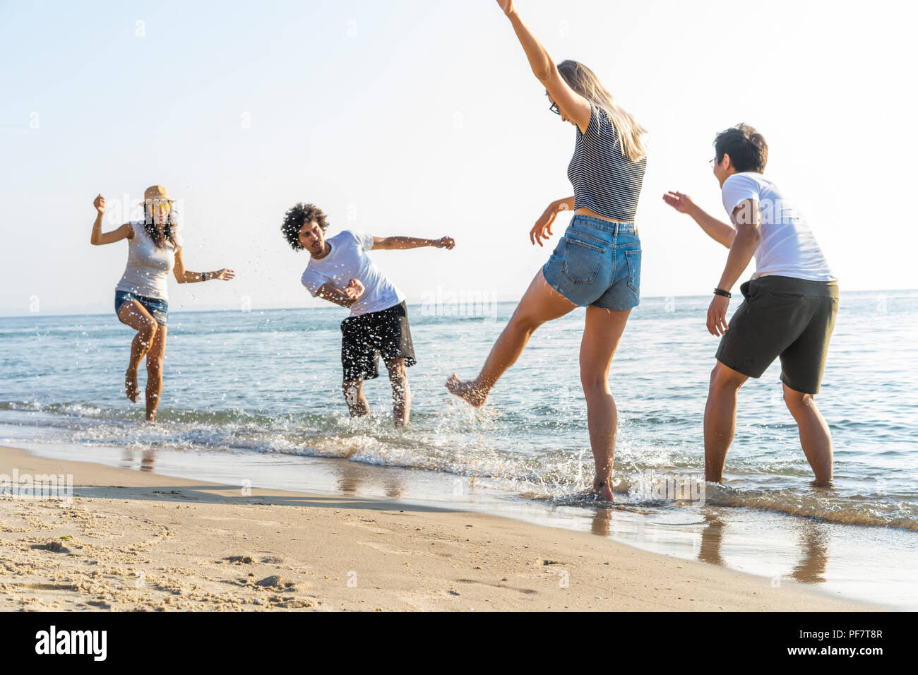 Group Of Friends Run Through Waves Together On Beach Vacation Stock ...