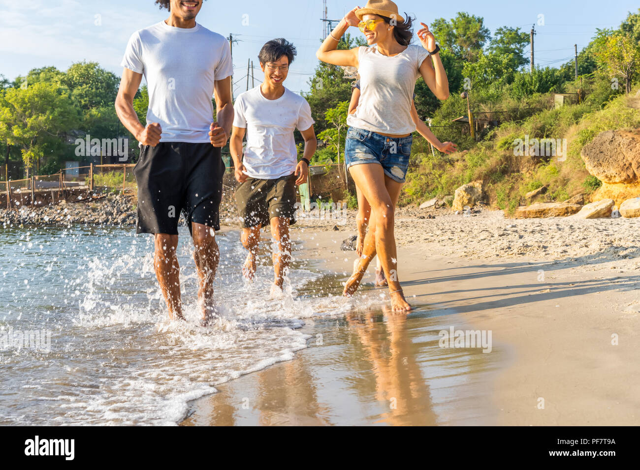 Group Of Friends Run Through Waves Together On Beach Vacation Stock ...