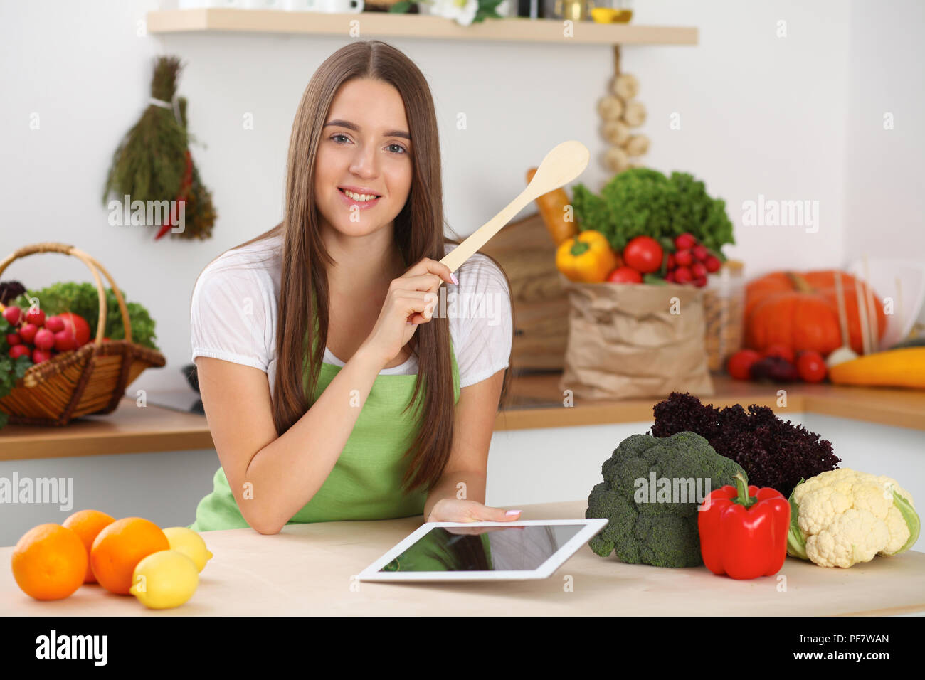 Young woman using tablet computer while cooking in kitchen ...