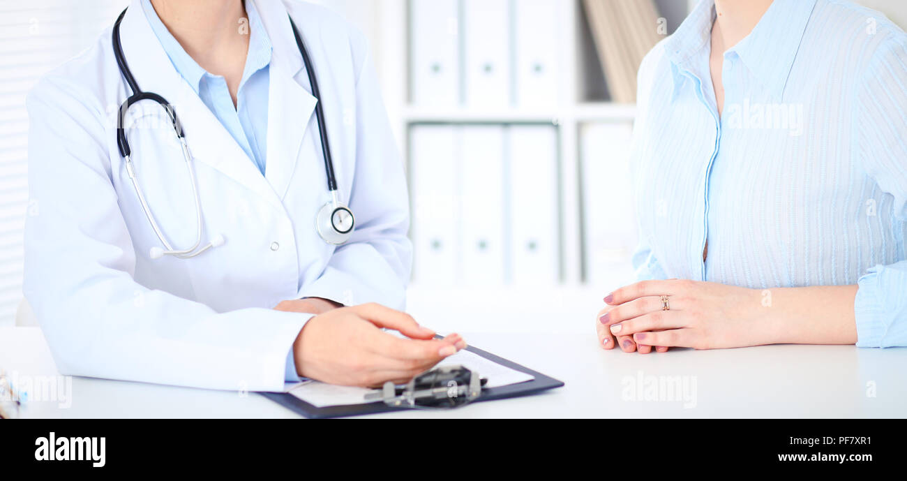 Unknown female doctor and patient discussing something while sitting at ...