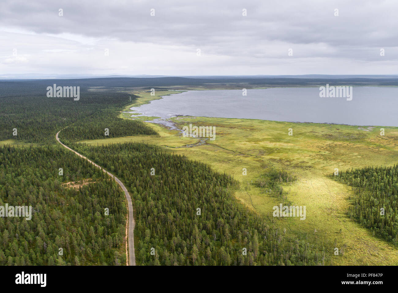 Aerial view of a dirt road and a lake in the middle of vast taiga ...