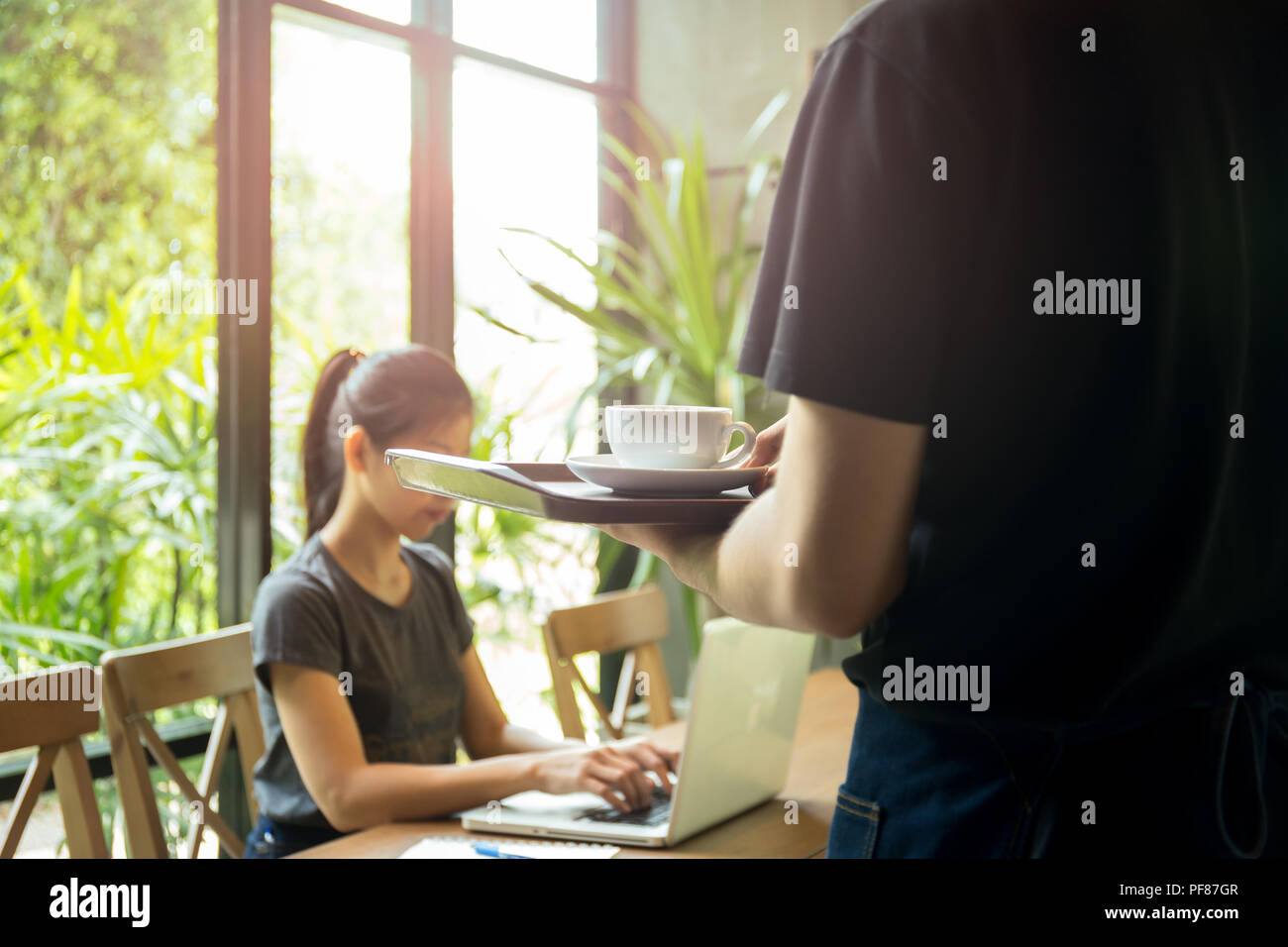 Woman working on laptop computer with waiter serving a cup of coffee in ...