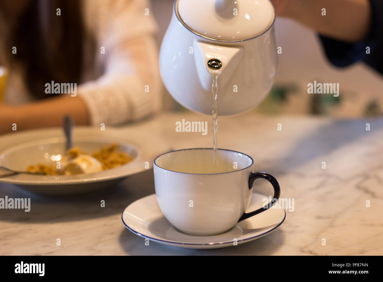 Hand pouring tea from teapot into tea cup on the table Stock Photo - Alamy