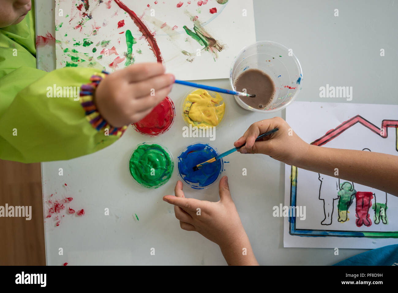 Young children painting with colourful acrylic paints viewed from above ...