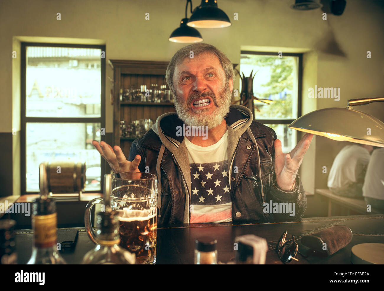 Angry bearded man drinking alcohol in pub and watching a sport program ...