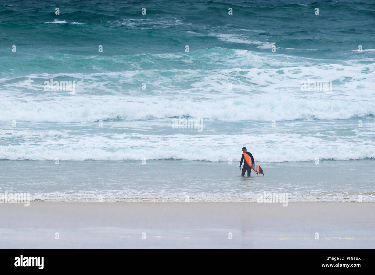 A tired surfer carrying his surfboard walking out of the sea at Fistral ...