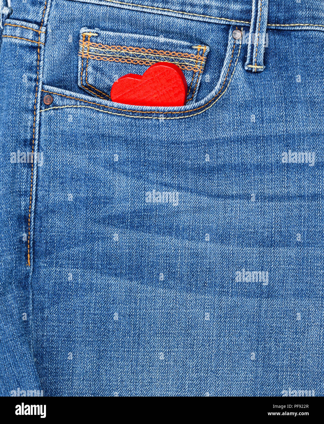 red heart lies in the front pocket of blue jeans, full frame, close up ...