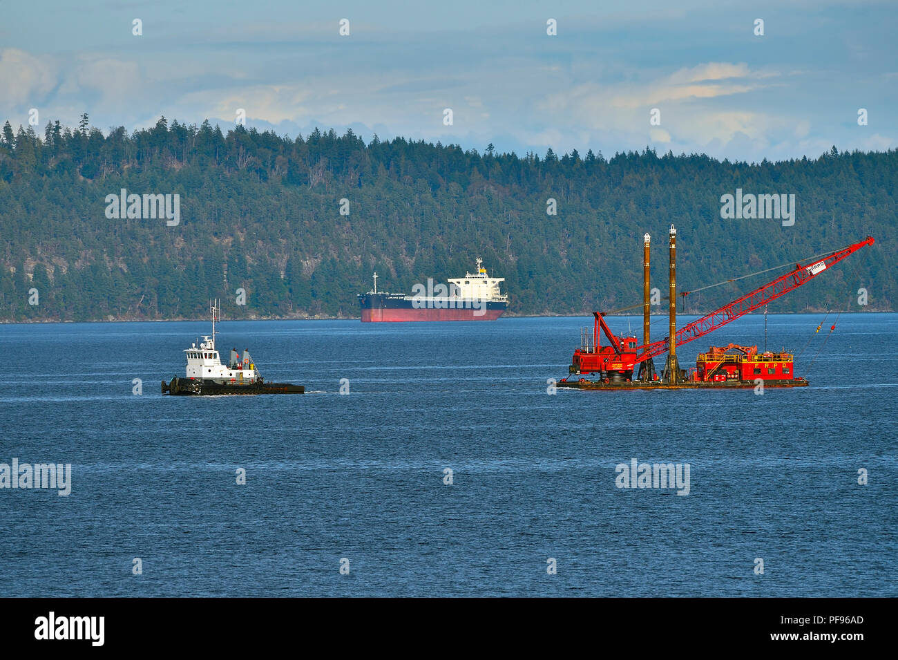 A tug boat pulling a heavy barge with a crane onboard through the ...