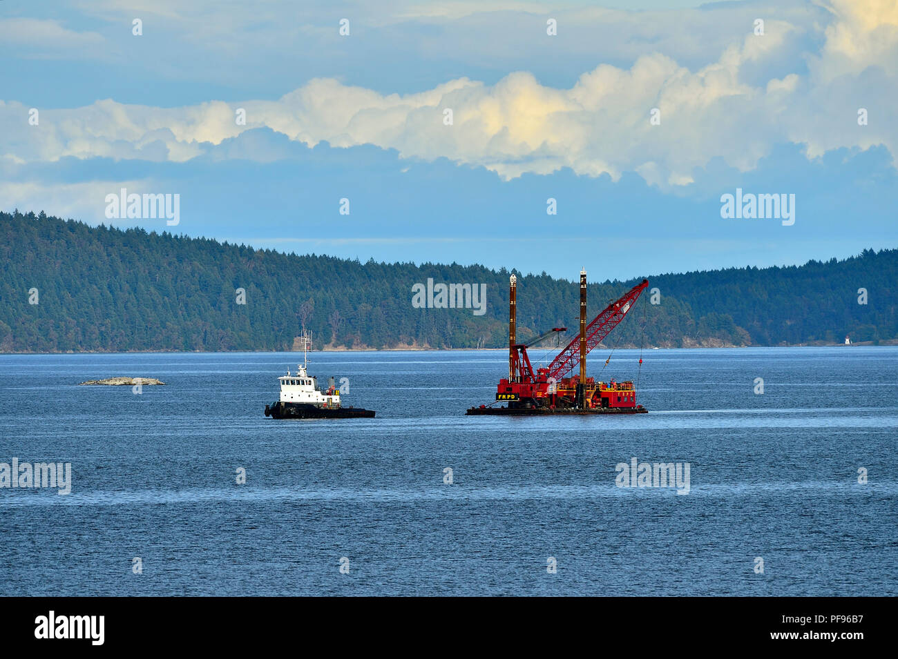 A tug boat hauling a barge with a crane onboard traveling through the ...