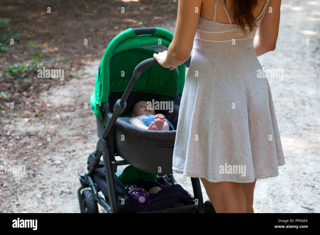Pretty woman in beautiful dress holding the pram with her happy cute ...