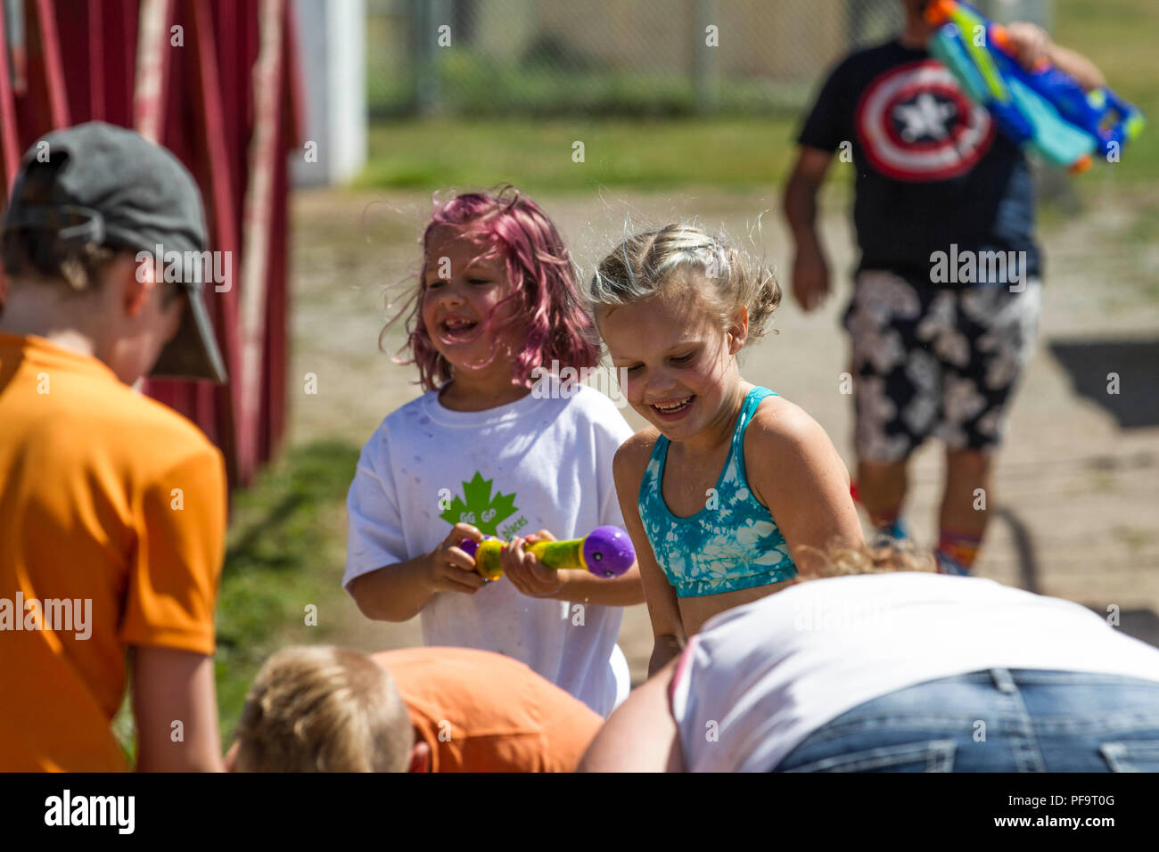 Summer time fun, kids and adults in a water fight. Smiling blonde and ...