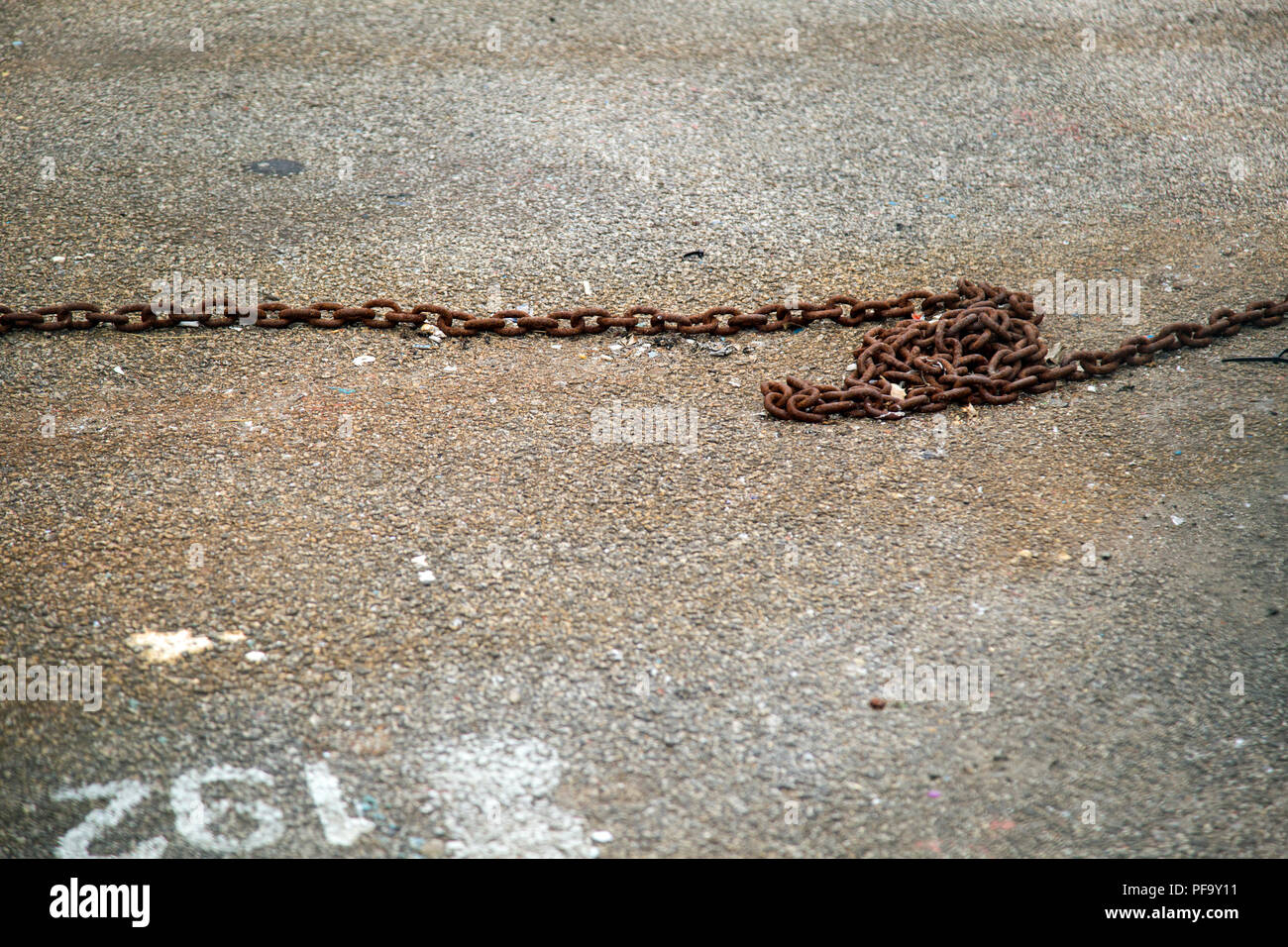 A single rusty chain on a concrete ground Stock Photo - Alamy