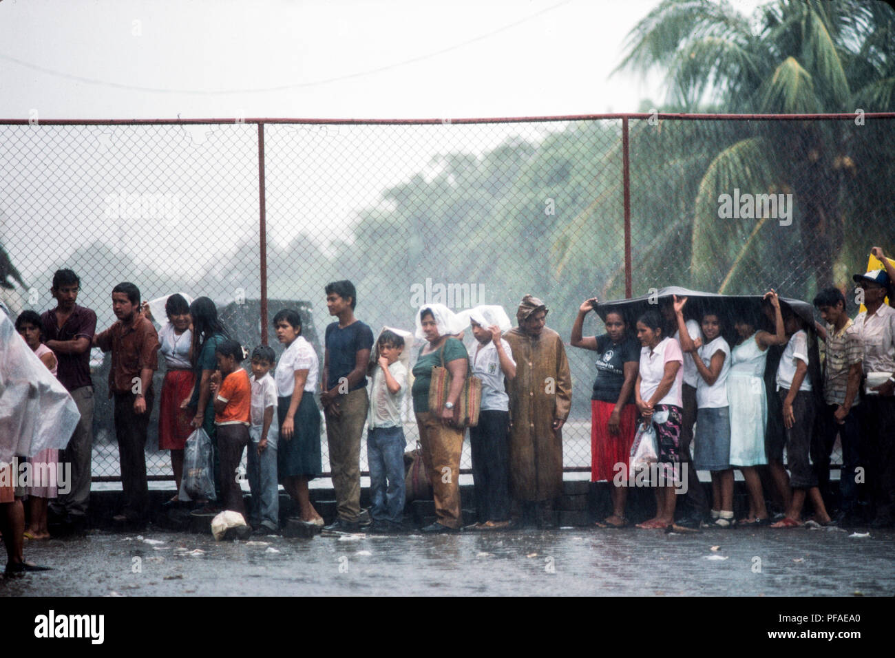 A group of people stand in heavy rain under makeshift coverings against ...