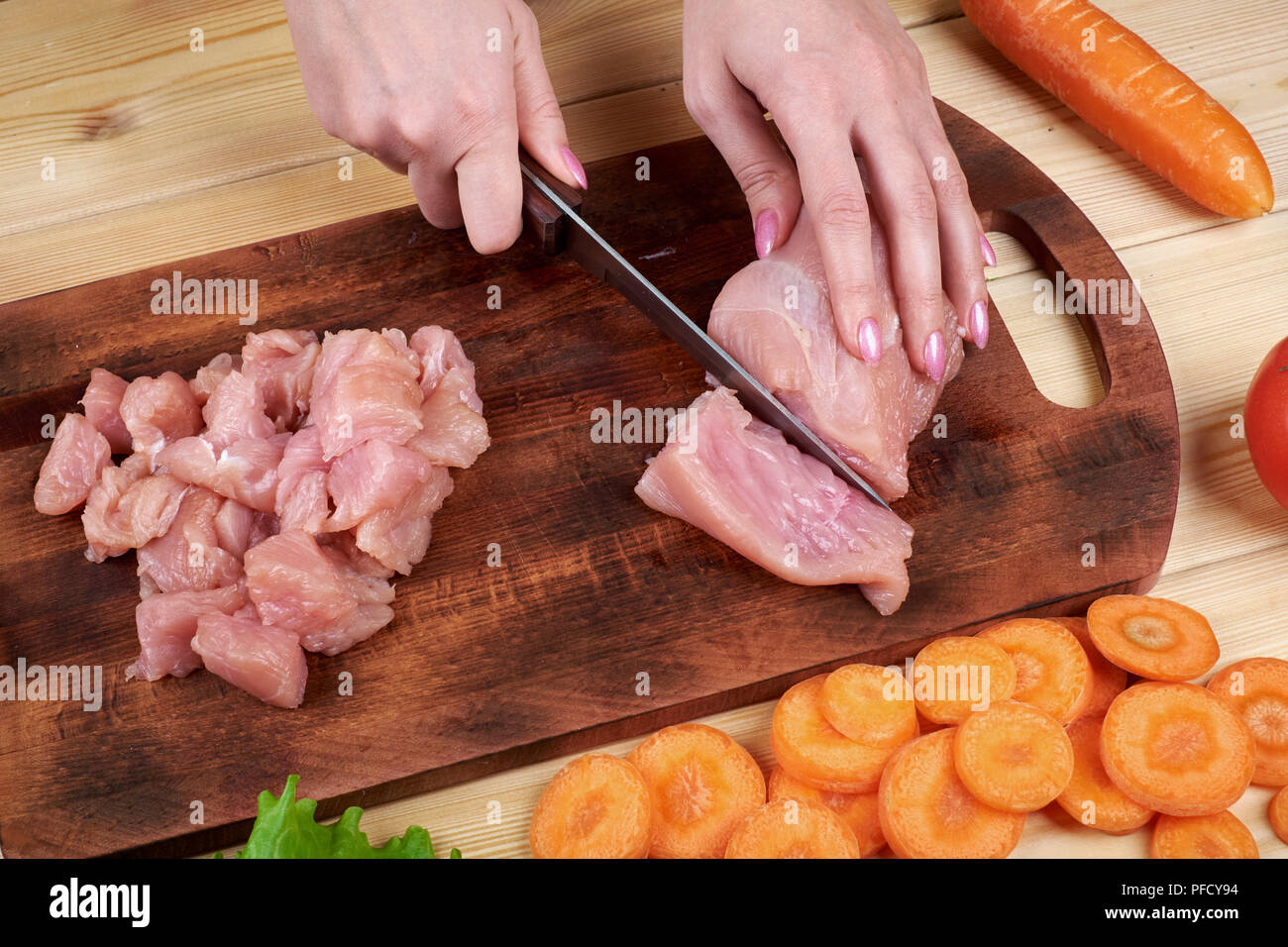 Female hands with a knife, cuts the meat on the wooden board . Healthy ...