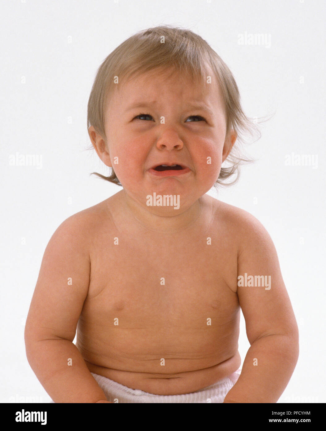 Baby wearing nappy, sitting on floor, crying, miserable expression ...