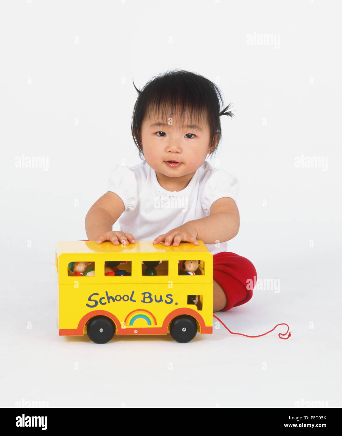 Baby girl in red trousers sitting on floor with yellow toy 'school bus ...