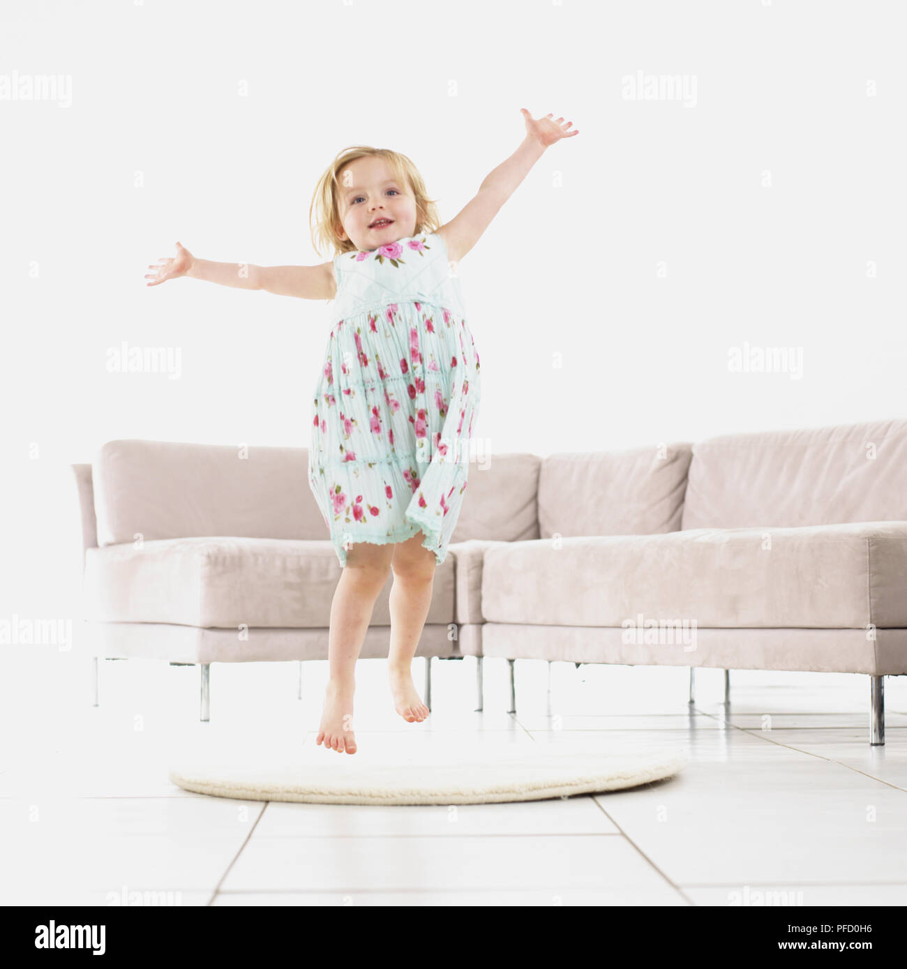 Girl jumping up from a rug in a living room with a sofa Stock Photo - Alamy
