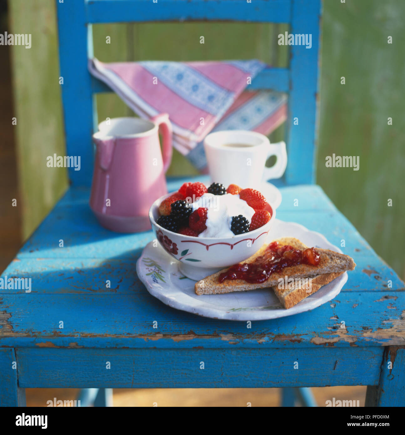 Breakfast laid out on blue wooden chair, bowl of strawberries and black ...