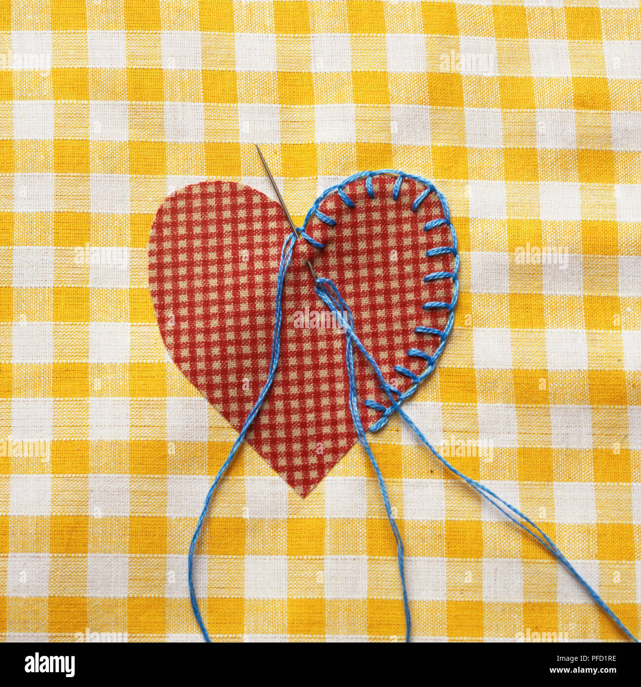 Hand sewing heart motif onto yellow gingham fabric using blanket stitch ...