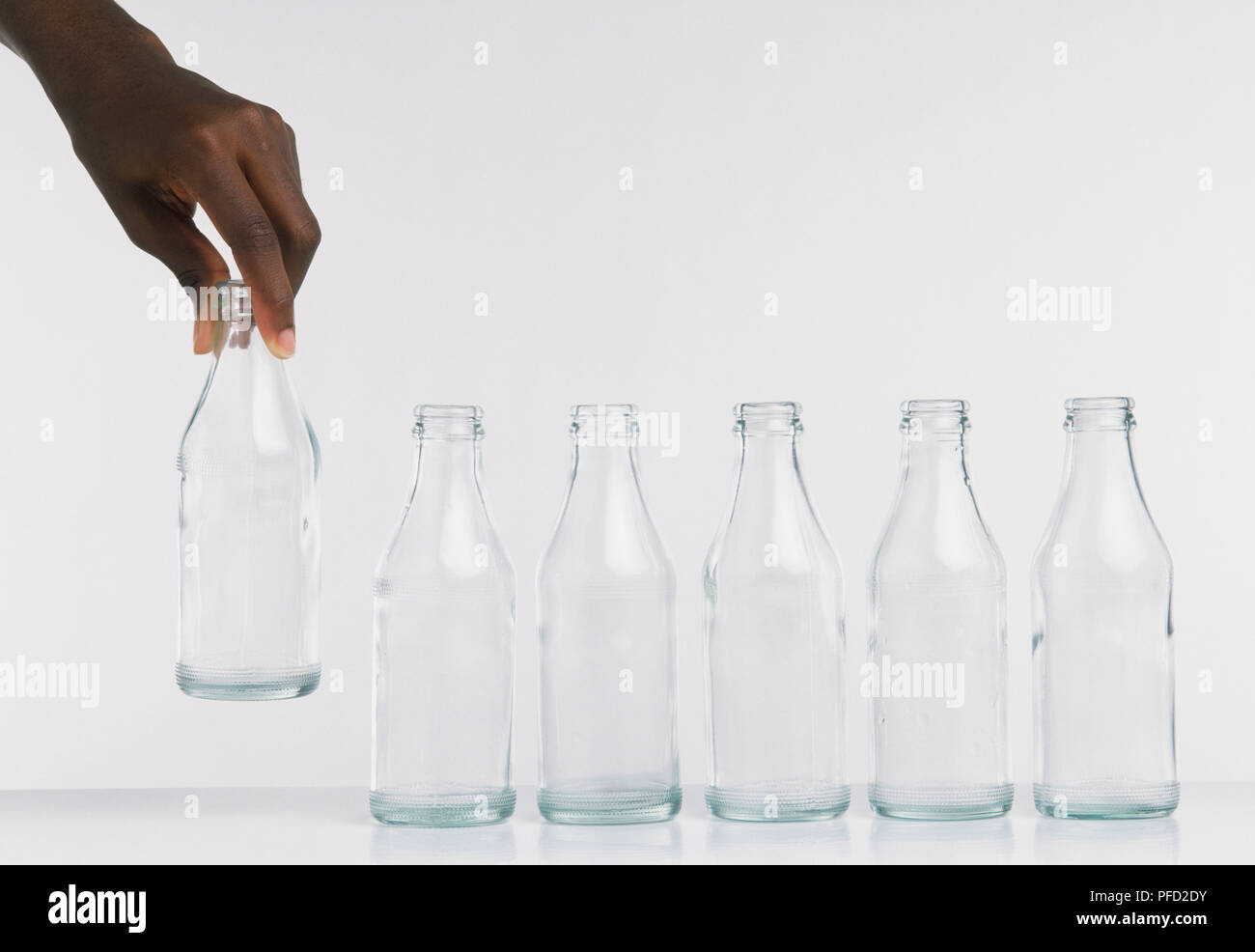Hand placing bottle next to five identical bottles, arranged in a row ...