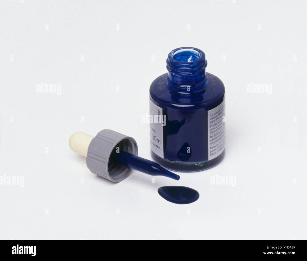 Bottle of blue ink, pipette, and drop of ink on white surface, close-up ...