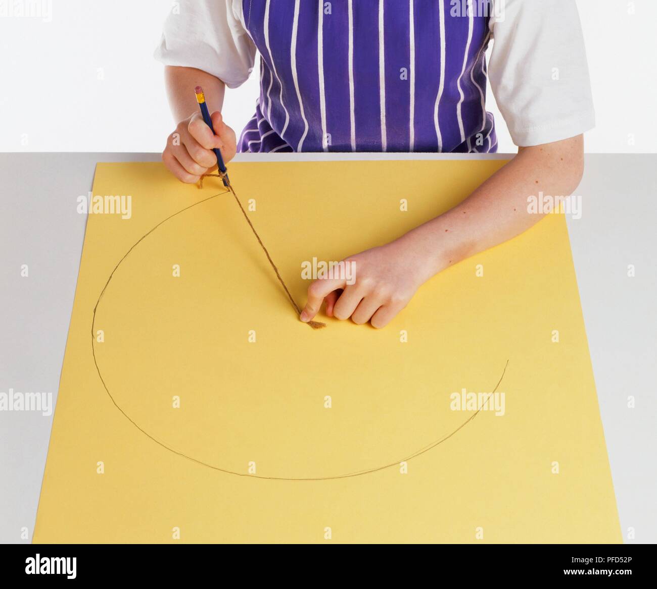 Child drawing circle on yellow paper using pencil tied to string Stock ...
