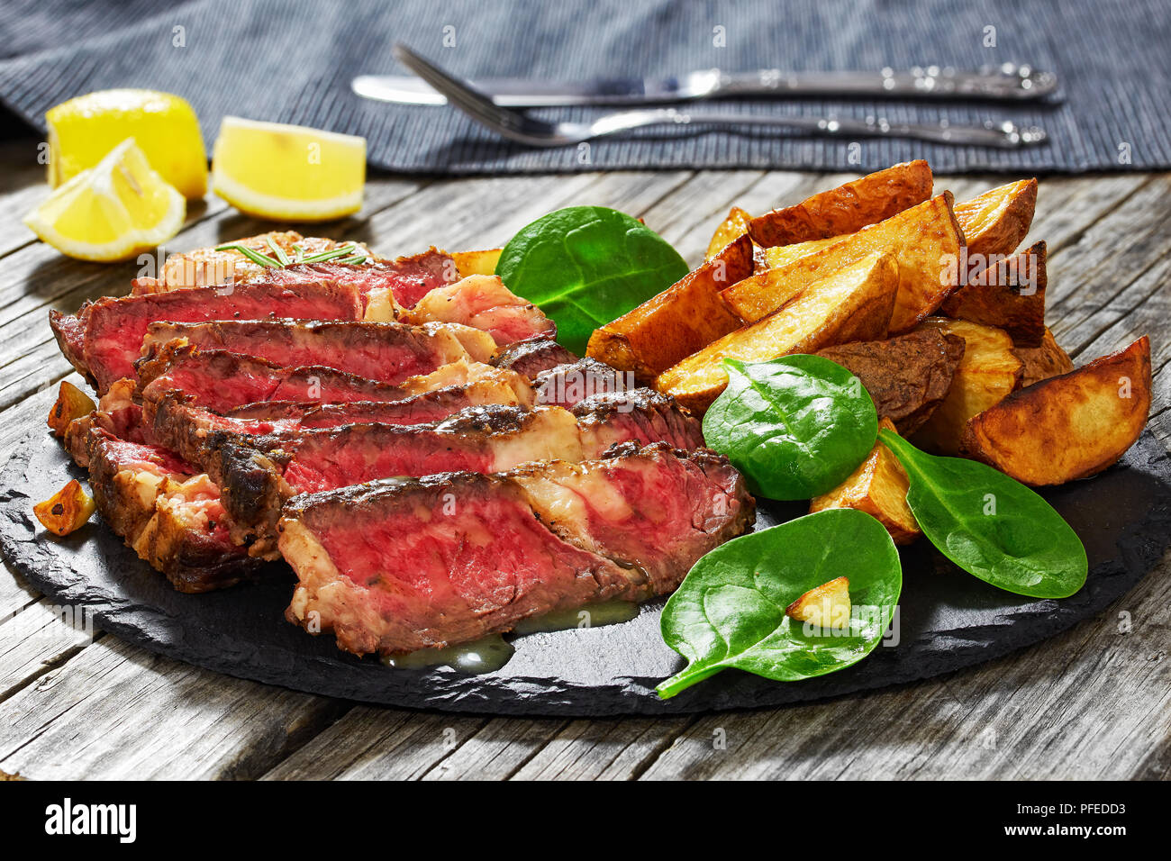 grilled medium-rare marbled ribeye steak cut in slices on slate plate ...