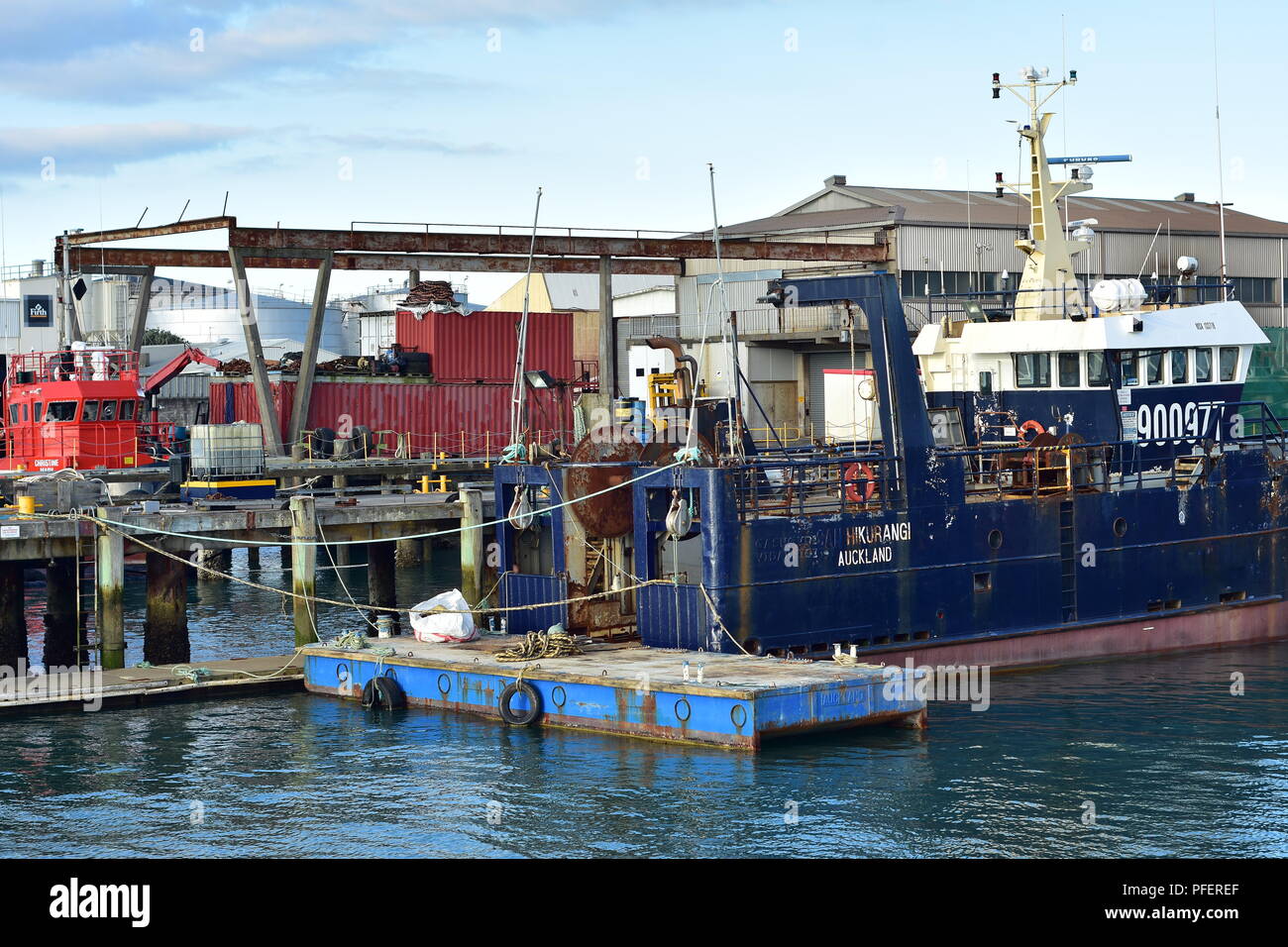 Rusty steel trawler with blue hull in port with small floating jetty at ...