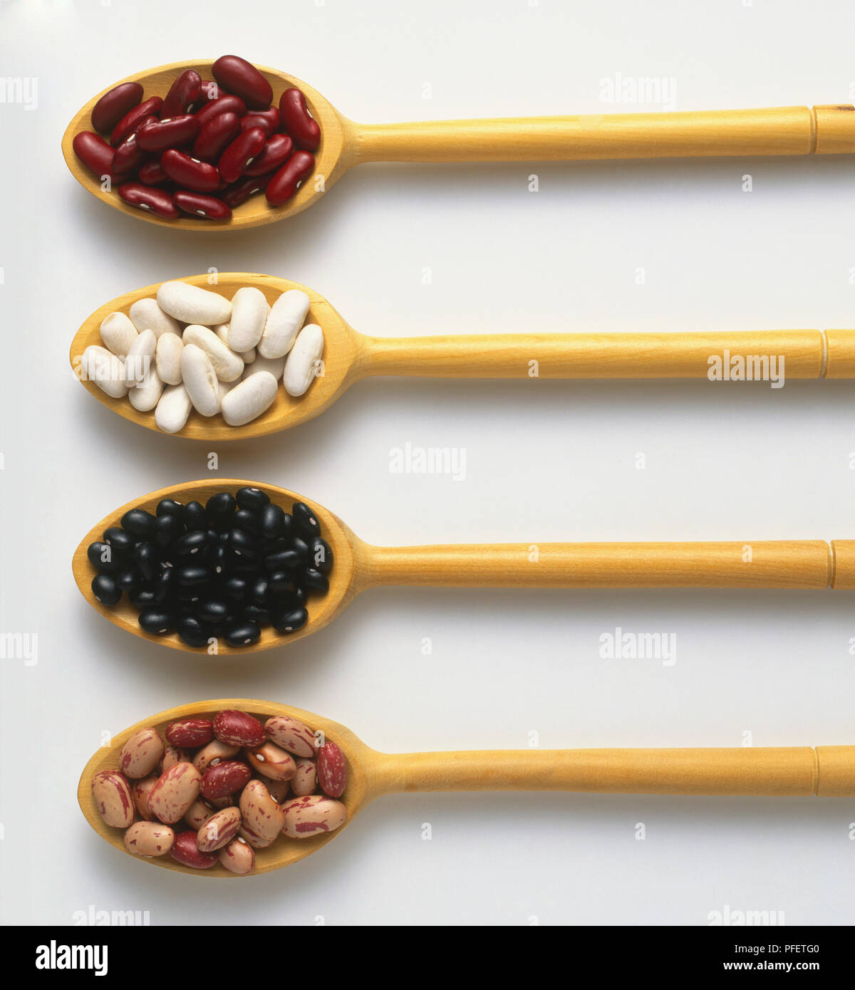 Four dried bean varieties presented on wooden spoons, red kidney beans ...