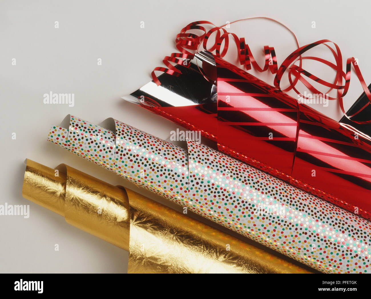 Rolled shiny gift-wrapping papers and curled red ribbon, side view ...