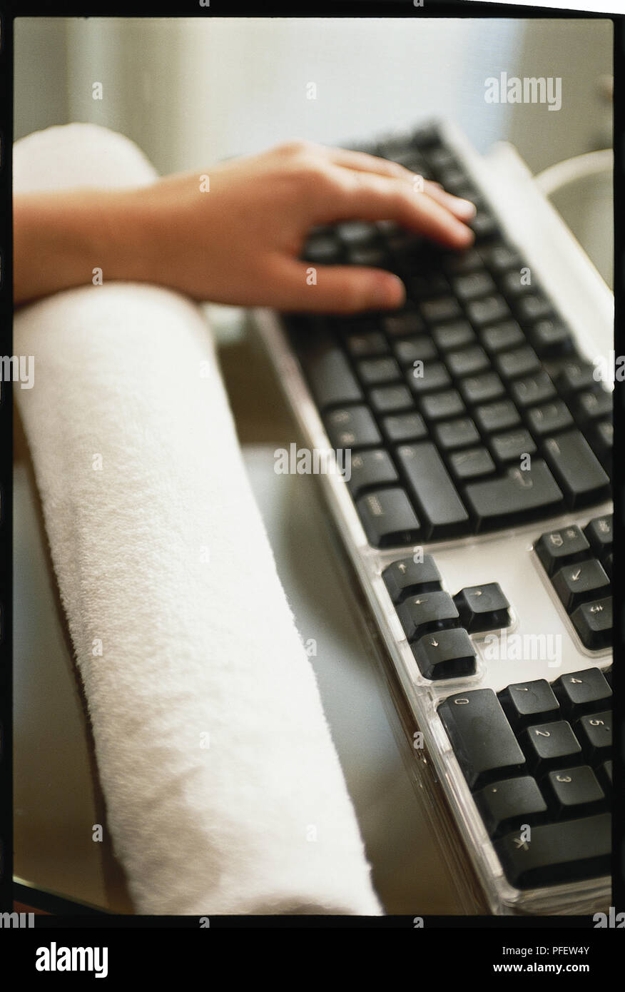Fingers typing on computer keyboard with wrist resting on rolled-up ...