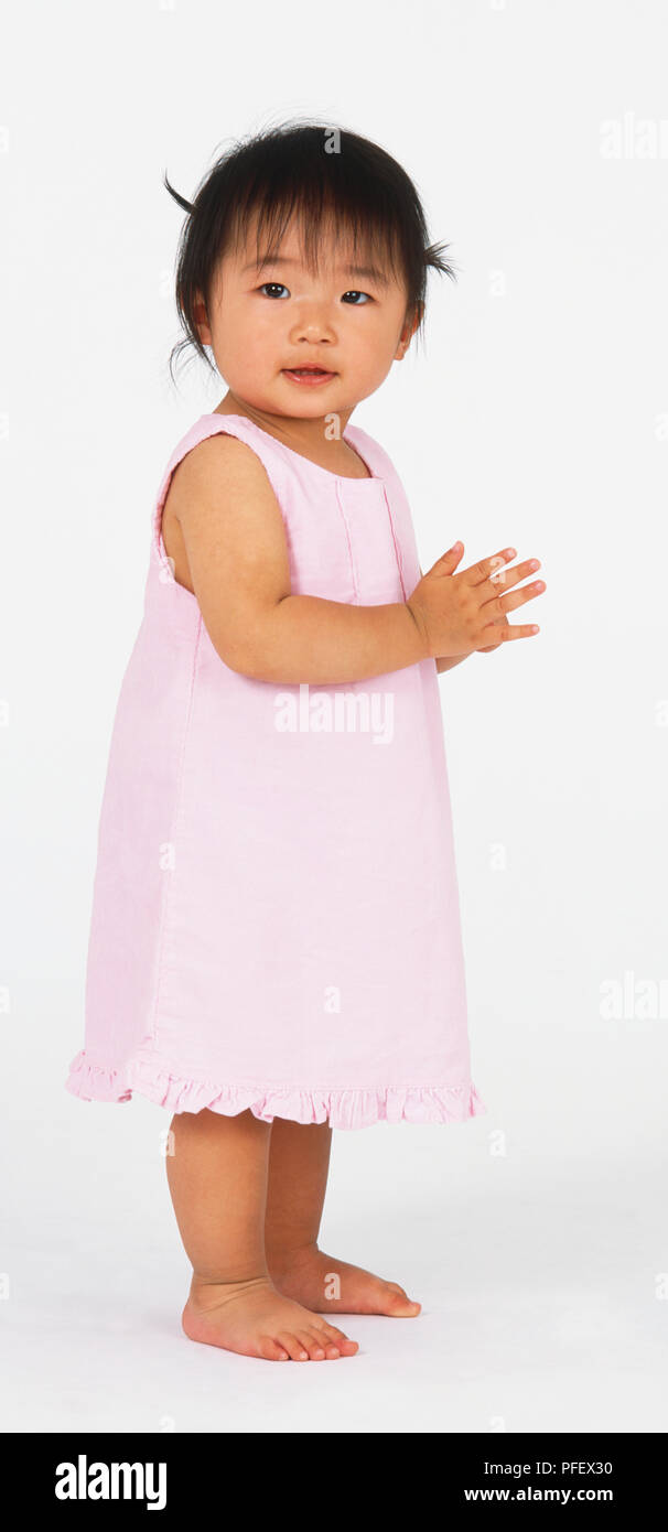 Girl toddler in pink dress standing and looking sideways, side view ...