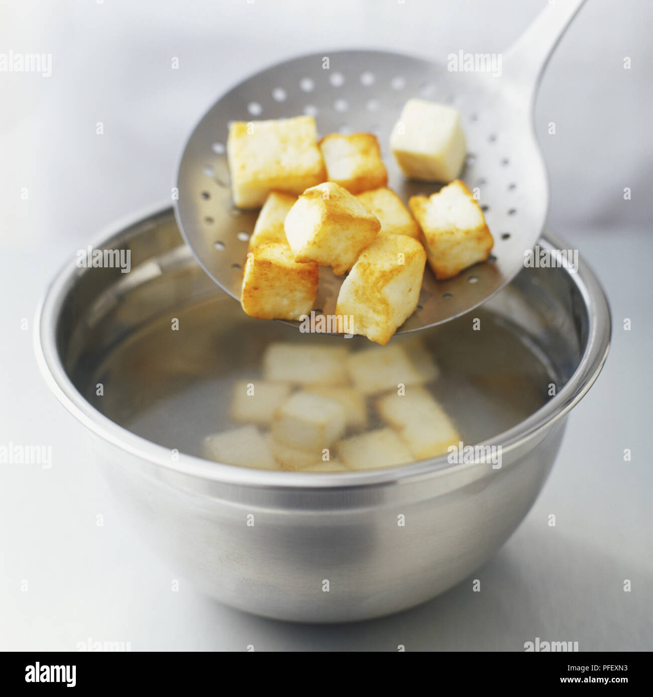 Cubes of deep-fried paneer cheese being spooned from a bowl of lukewarm ...
