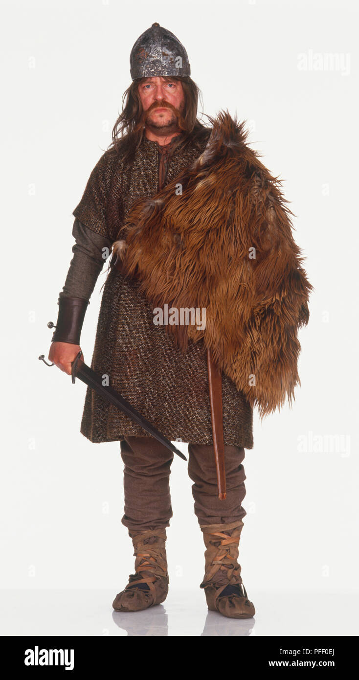 Man wearing Viking costume, sword in hand and animal skin over shoulder ...