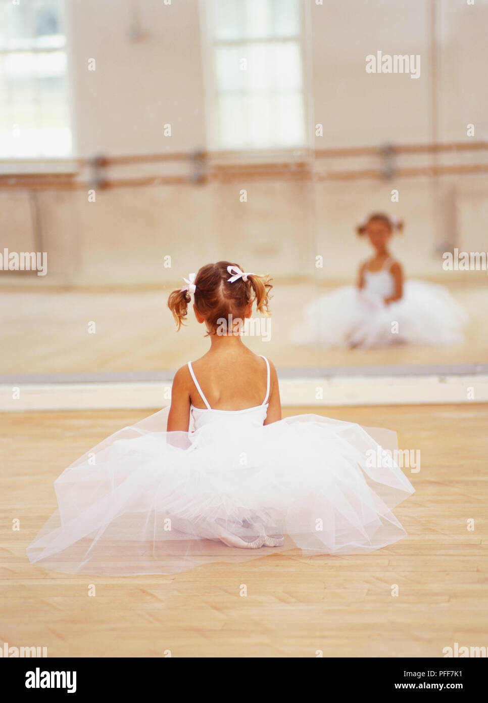 Young dancer wearing white leotard and tutu sitting on wooden floor ...